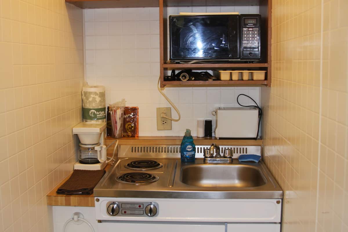 Uma cozinha compacta com micro-ondas, fogão, pia e cafeteira.
