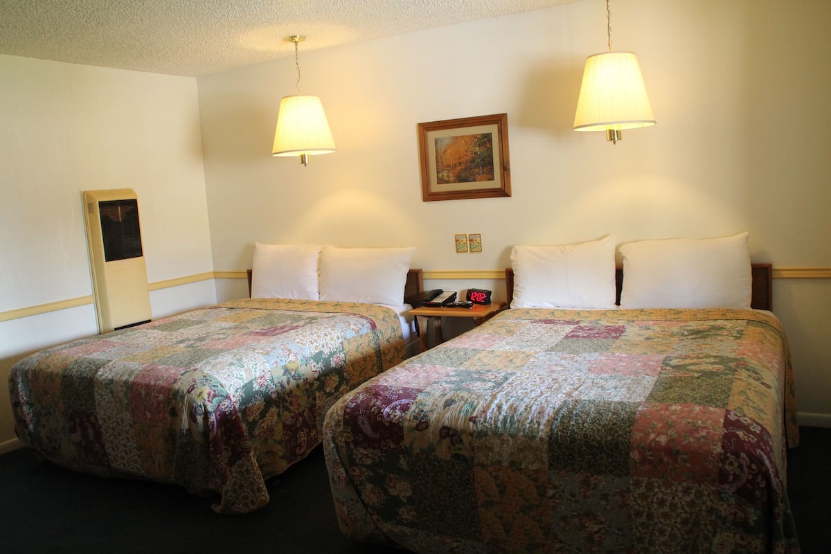 Quarto de hotel com duas camas de solteiro, cada uma com edredom floral, mesa de cabeceira com abajur e um quadro na parede.