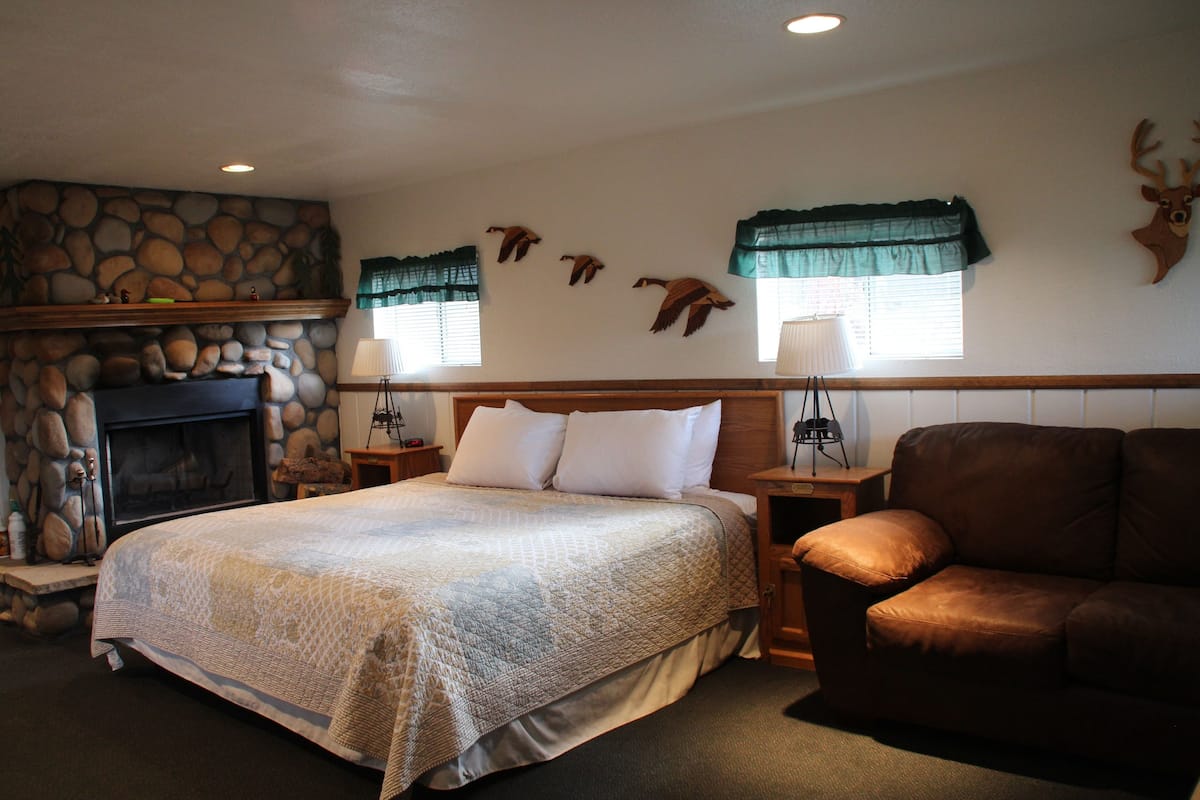 Quarto com cama grande, lareira de pedra, poltrona de couro e decorações de animais nas paredes.