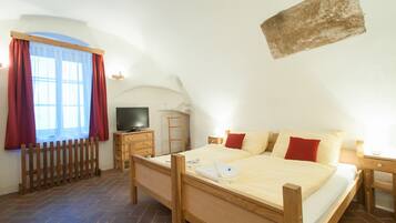 Quarto com cama de madeira, televisão, mesa de cabeceira de madeira e janela com cortinas vermelhas.