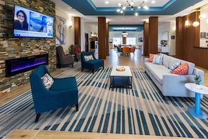 Um saguão de hotel com uma televisão exibindo notícias, uma lareira, áreas de estar e um espaço de refeições.