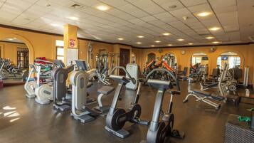 Uma academia com diversos equipamentos de exercício, uma lousa com uma lista e um relógio na parede.