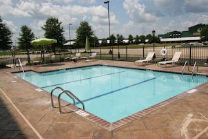 Piscina retangular com deck ladrilhado, cercada por uma grade de metal e equipada com espreguiçadeiras e guarda-sóis.