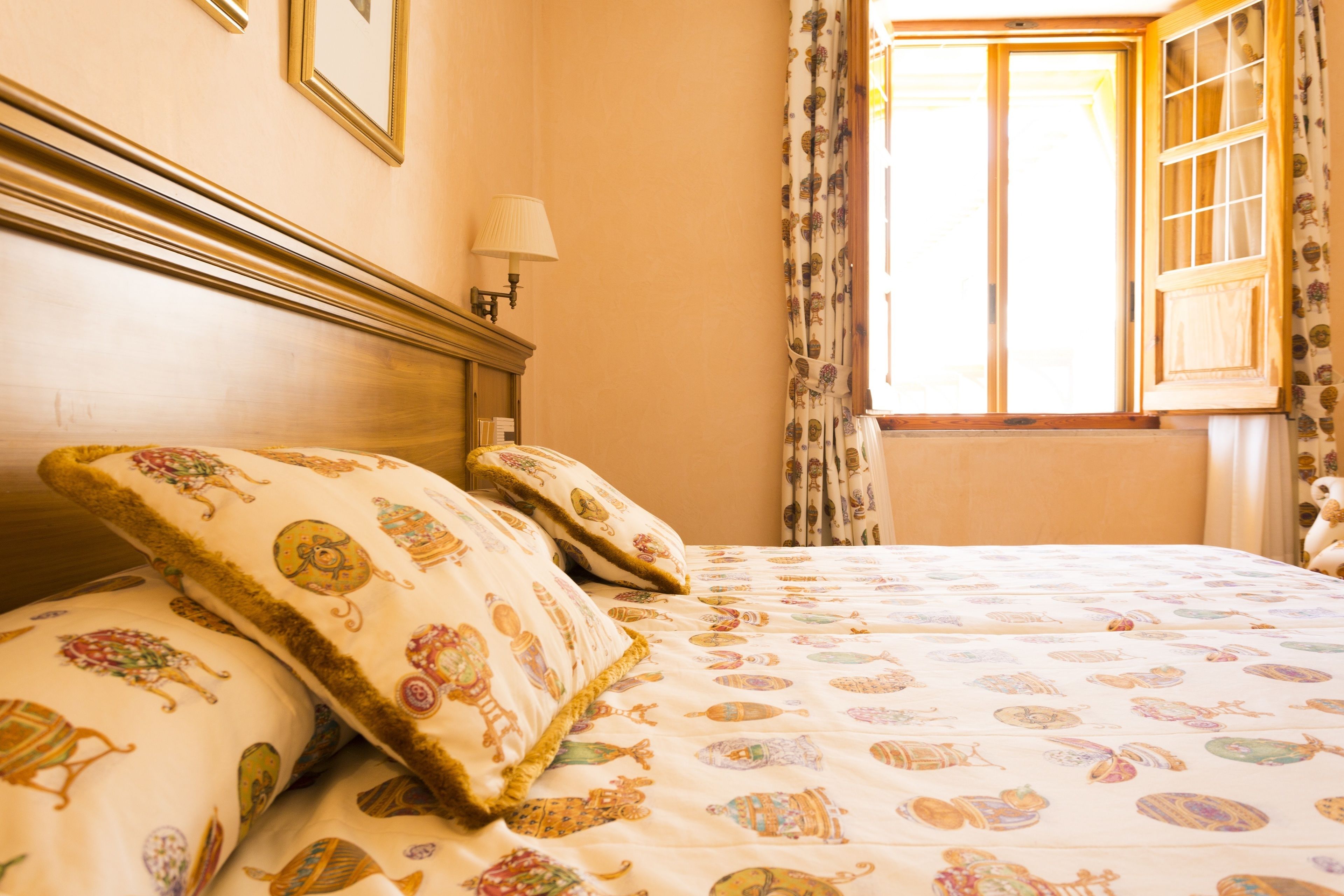 Quarto de hotel com uma cama grande, cabeceira elaborada e janela com cortinas.