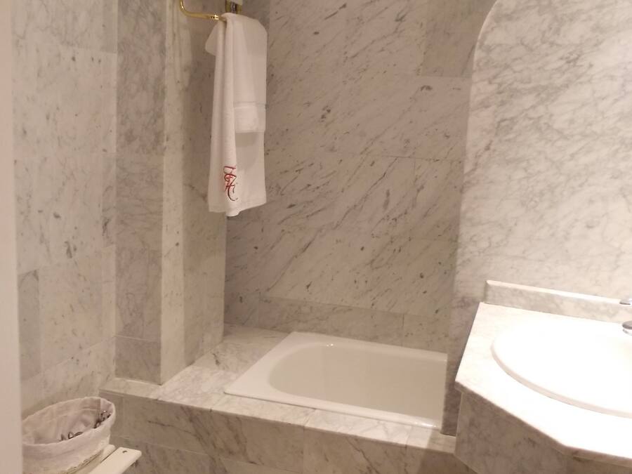 Casa de banho com chão de mármore, uma banheira, lavatório e porta-toalhas.