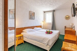 Quarto de hotel com uma cama, mesa de cabeceira de madeira, escrivaninha, cadeira, espelho e janela com cortinas.