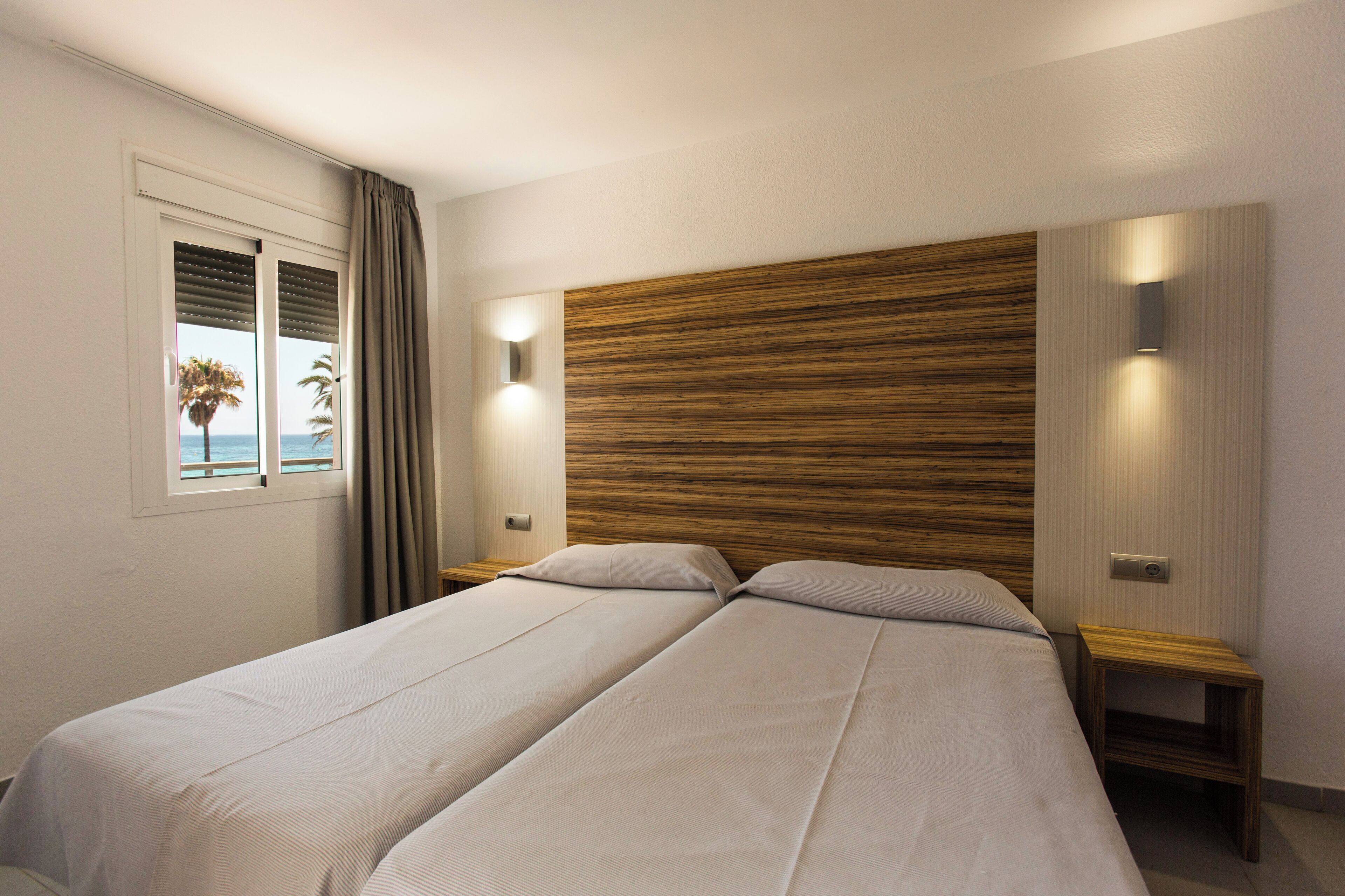 Uma cama de casal com cabeceira de madeira, mesas de cabeceira e uma janela com cortinas.