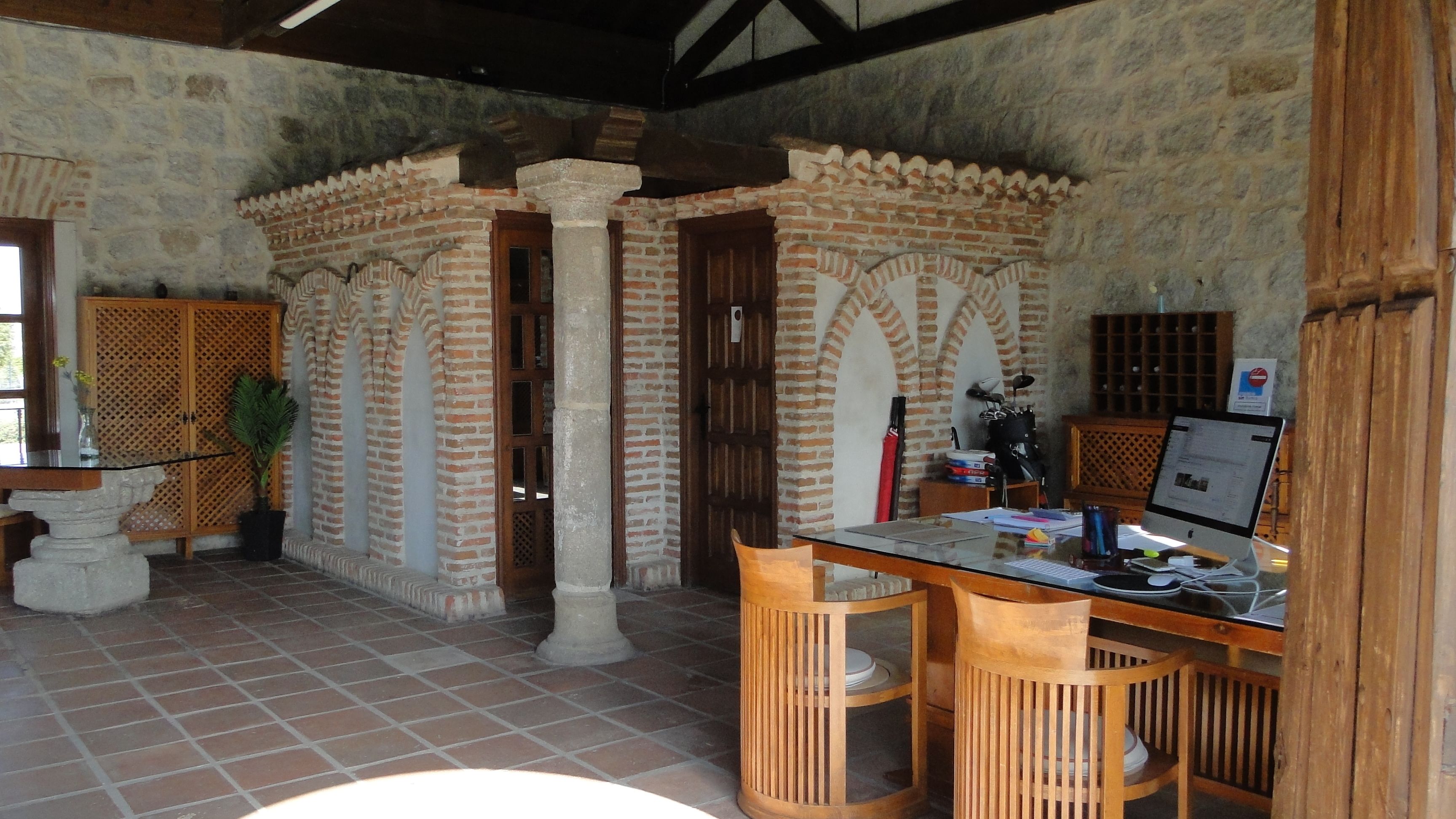 Um interior rústico com parede de pedra, portas de madeira, soalho em azulejos e uma mesa com cadeiras.