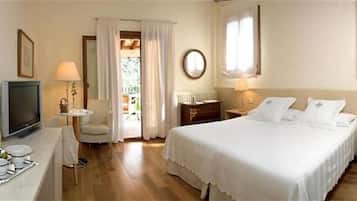 Quarto de hotel com cama, escrivaninha com televisão, cadeira, mesa com abajur e janela com cortinas.