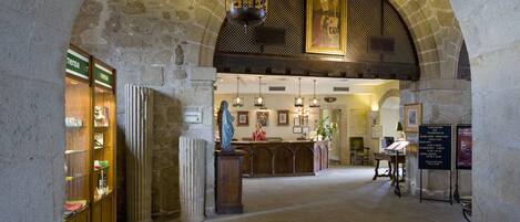 Um hall com paredes de pedra, uma mesa de recepção, uma estátua e um lustre.