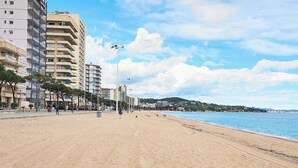 Uma praia com uma fileira de edifícios altos, céu claro e mar calmo.