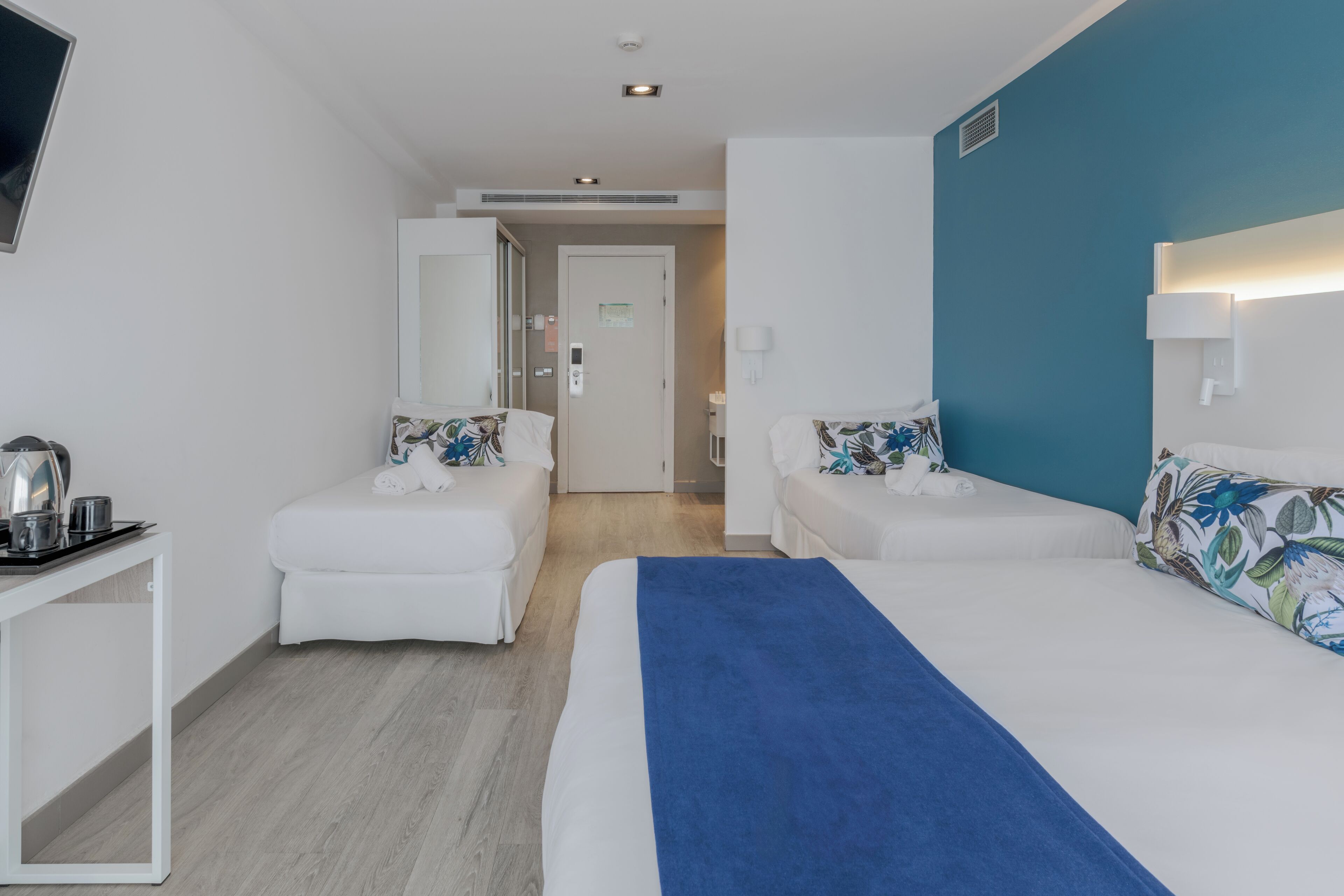 Quarto de hotel com duas camas, televisão, escrivaninha e cafeteira.