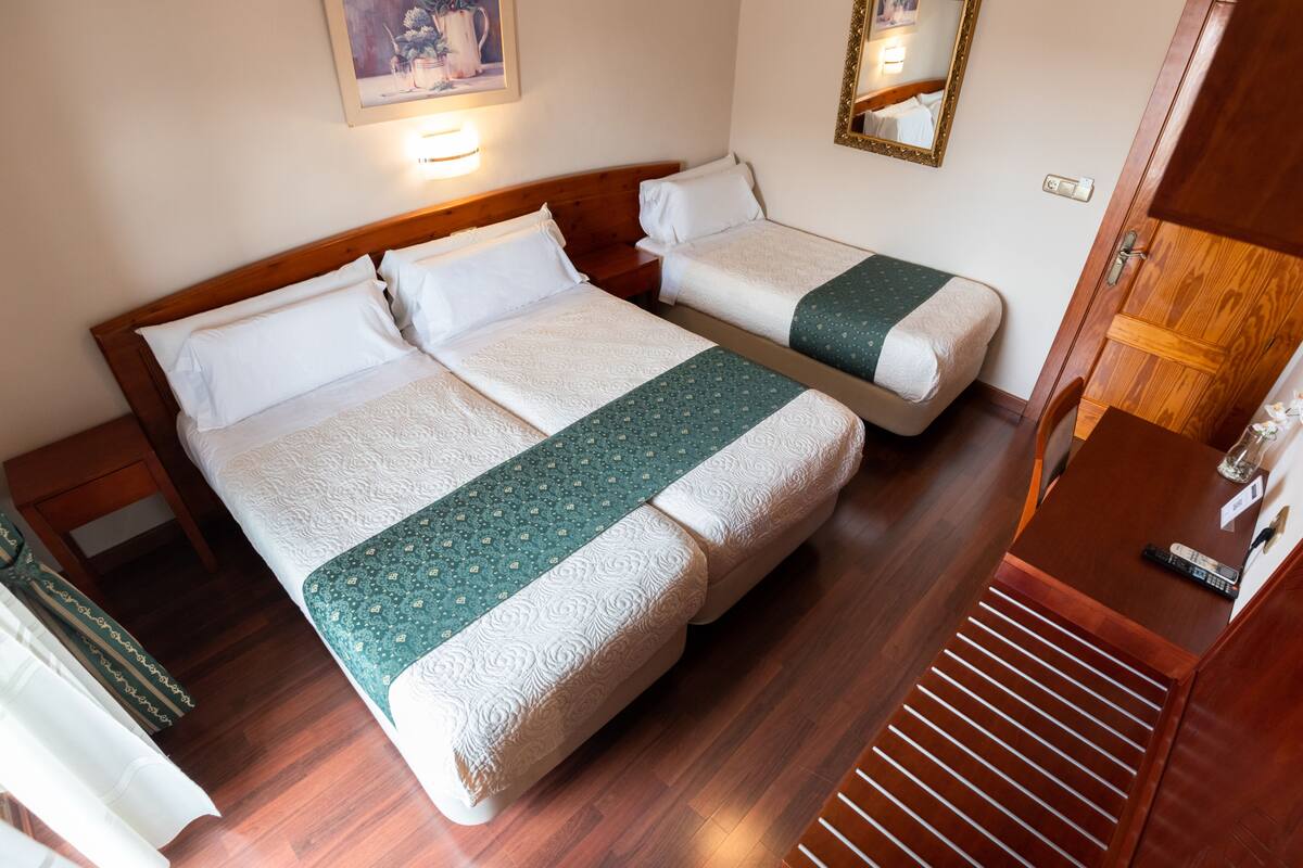 Quarto de hotel com duas camas, cabeceiras de madeira, mesa de cabeceira, espelho e cômoda de madeira.