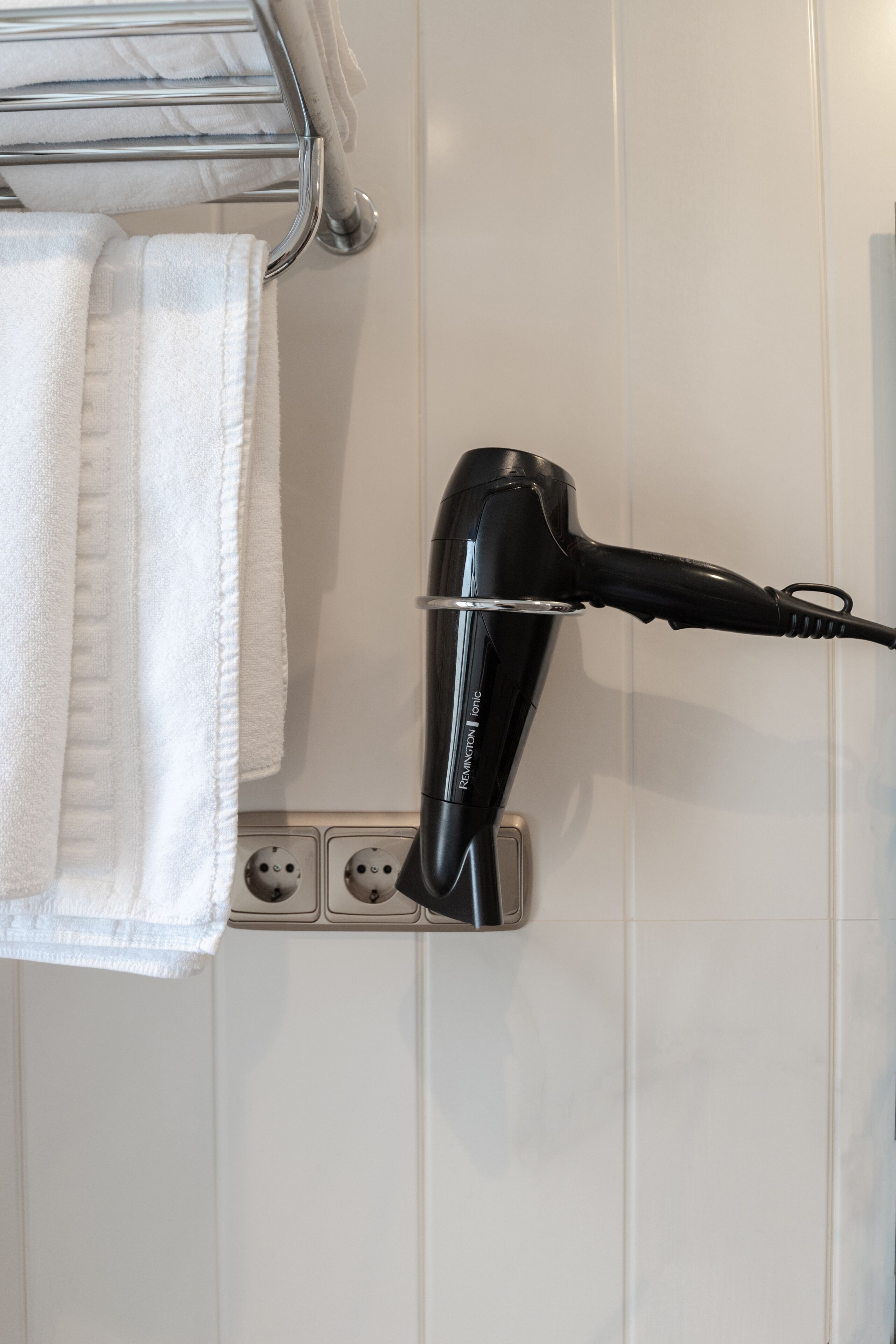 Um secador de cabelo fixado na parede próximo a um porta-toalhas.