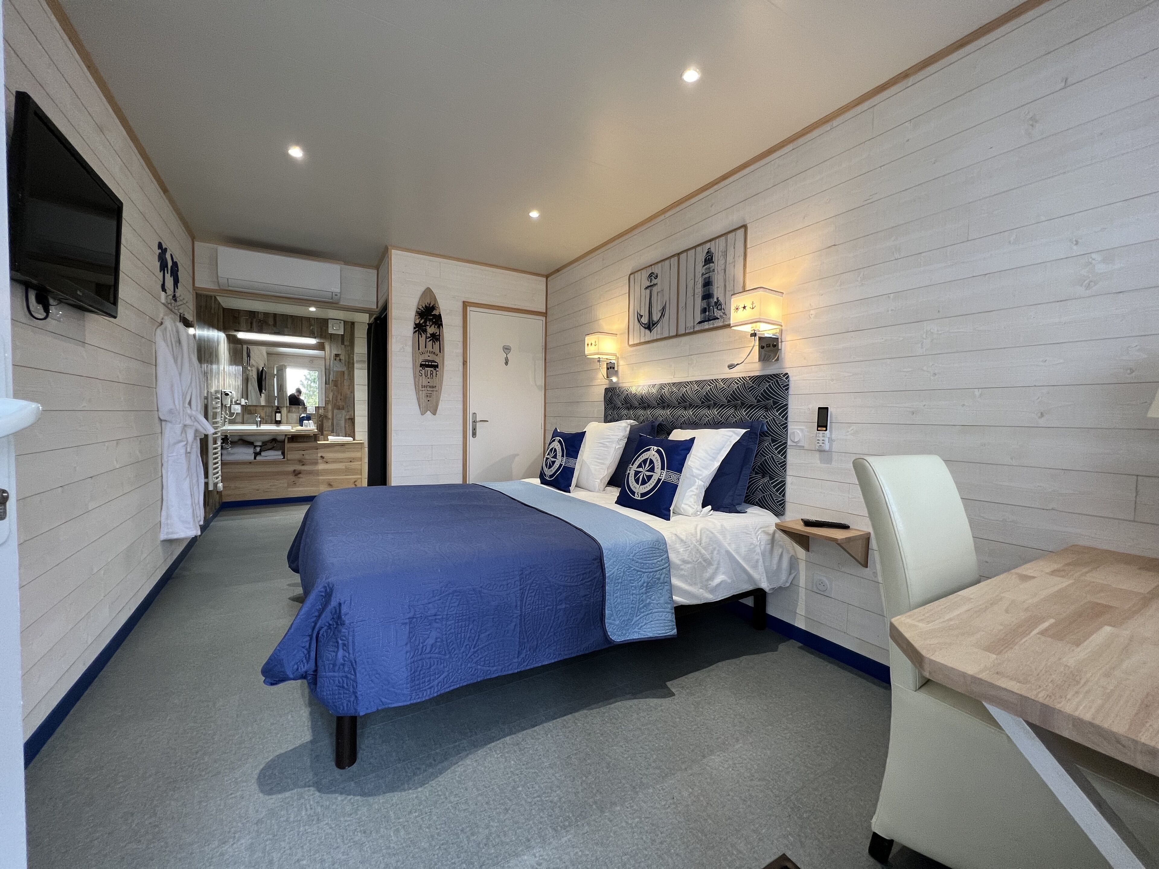 Quarto de hotel com uma cama, uma escrivaninha e um banheiro visível ao fundo.