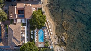 Vista aérea de uma propriedade costeira com piscina, acesso à praia e uma linha costeira rochosa.