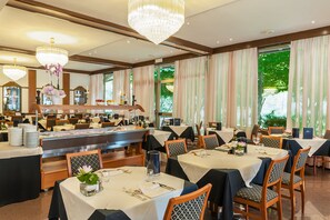 Restaurante com várias mesas, cadeiras e uma área central para buffet.