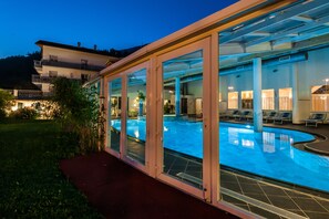 Piscina com portas de vidro, área coberta com espreguiçadeiras e um edifício ao fundo.