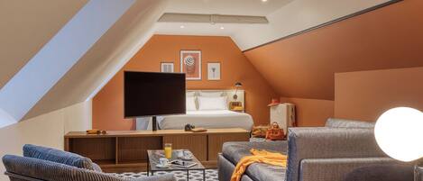 Quarto moderno e compacto com pé-direito estilo loft, cama, escrivaninha, televisão e áreas de estar.