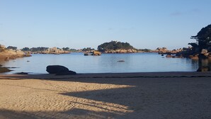Uma praia arenosa com águas calmas, grandes rochas e uma ilha distante coberta de árvores.