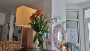 Um quarto com uma cesta trançada, um vaso com flores, uma mesa de cabeceira de madeira, um espelho fixado na parede e um mapa na parede.