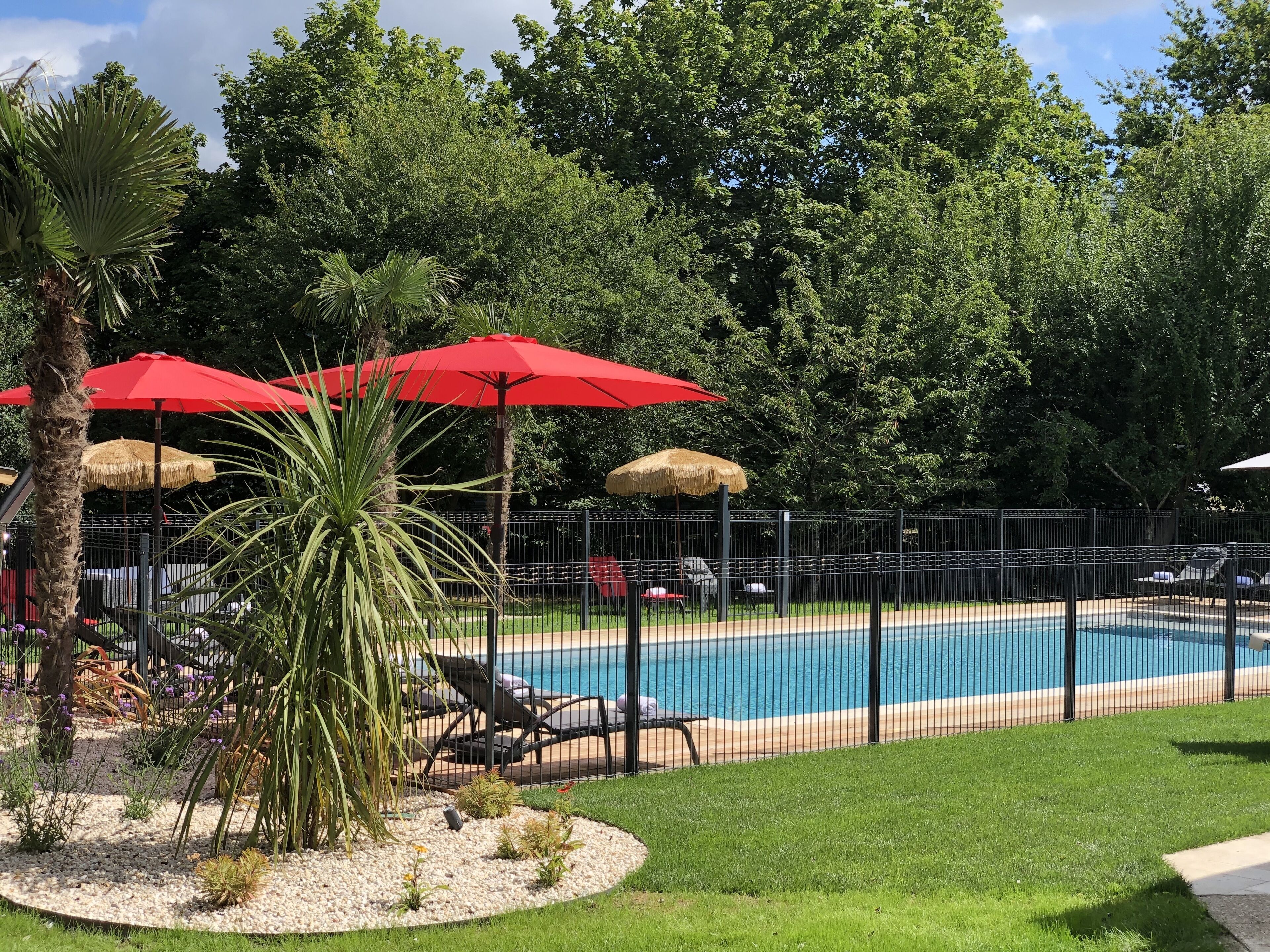 Piscina cercada por grade, com cadeiras de descanso e guarda-sóis.