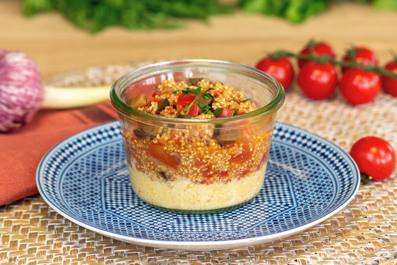Uma tigela de vidro com salada de quinoa sobre um prato azul estampado.