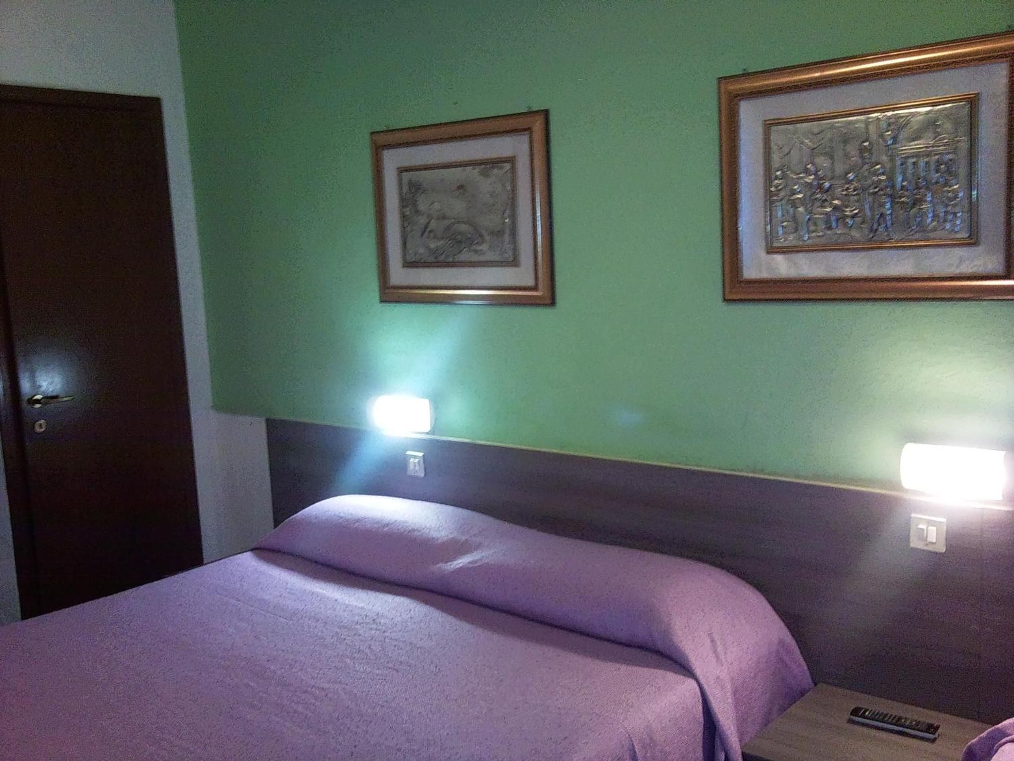 Quarto com cama, duas luminárias na parede e duas fotos emolduradas.