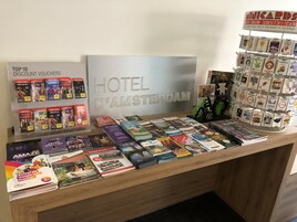 Bancada de recepção de hotel com uma exposição de vales de desconto, uma placa para Hotel d'Amsterdam e um suporte com folhetos de viagem.
