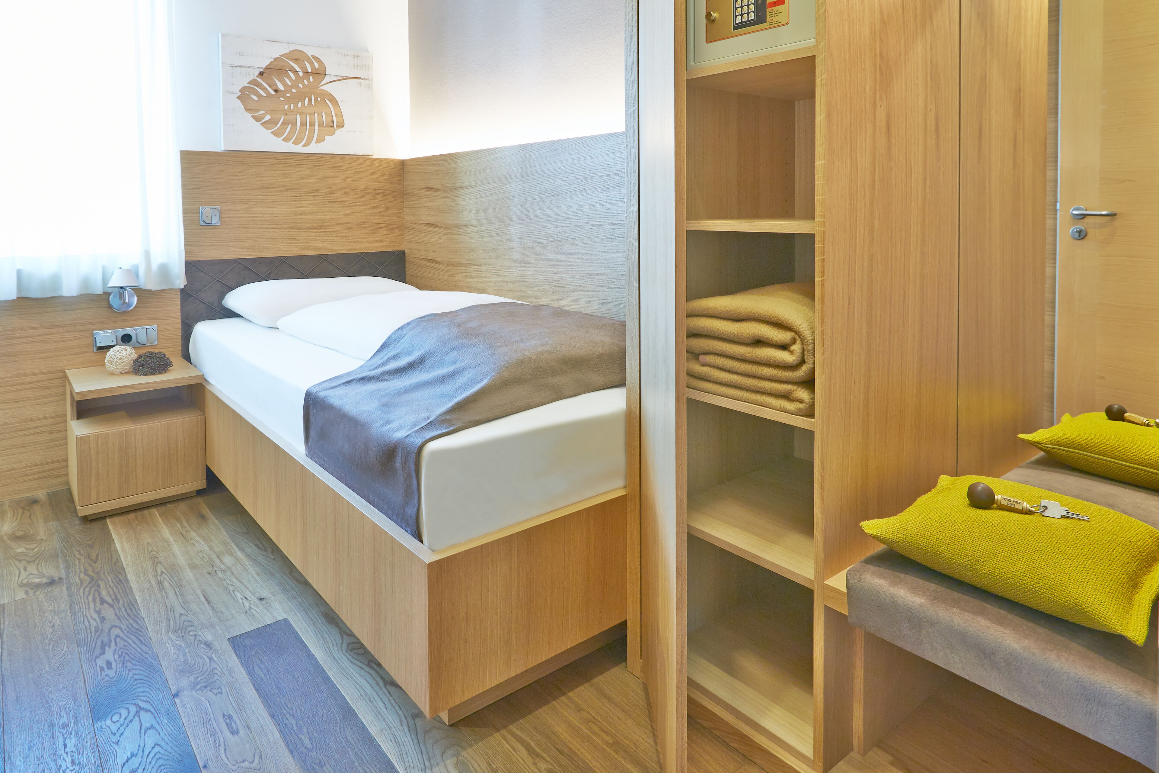Quarto moderno com cama de madeira, mesa de cabeceira, guarda-roupa e um banco com toalhas.