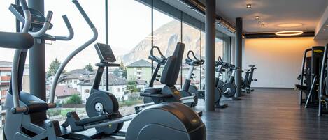 Uma academia com equipamentos de cardio e vista para montanhas através de grandes janelas.