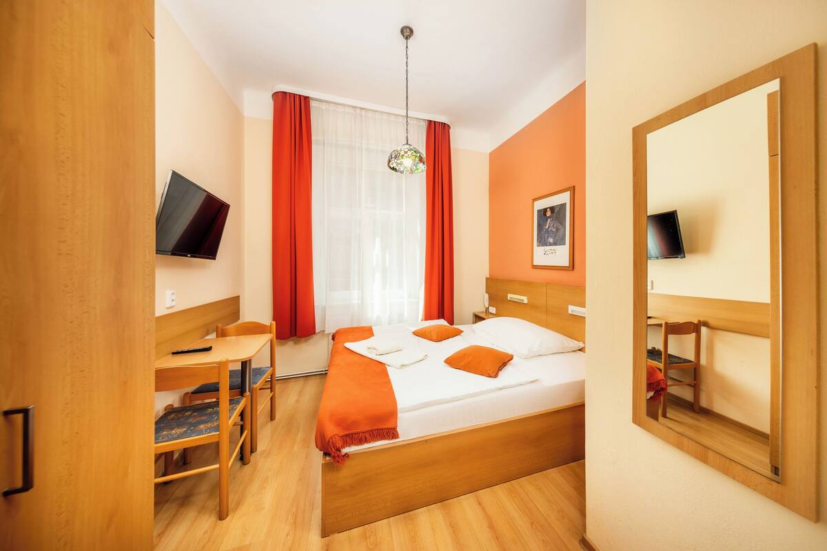 Quarto de hotel com cama de madeira, uma escrivaninha com cadeira, televisão e um espelho grande.