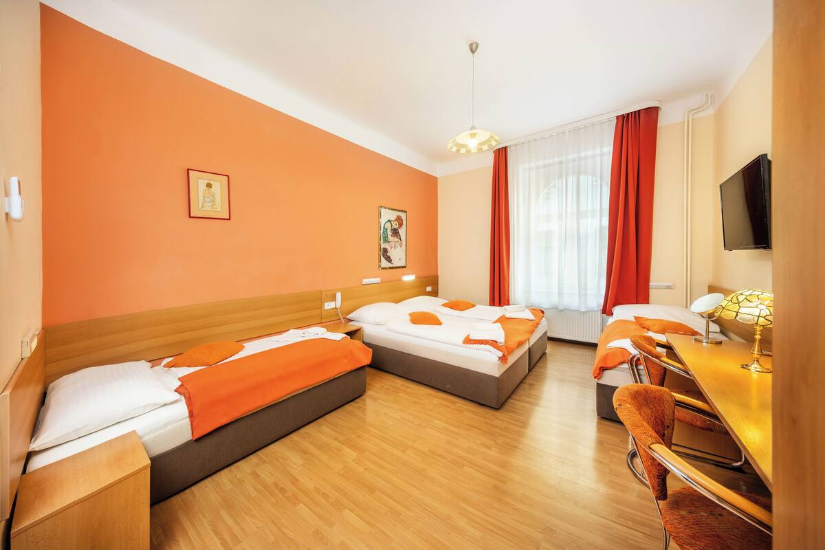 Quarto de hotel com duas camas, uma mesa, uma cadeira, uma televisão e uma janela com cortinas.
