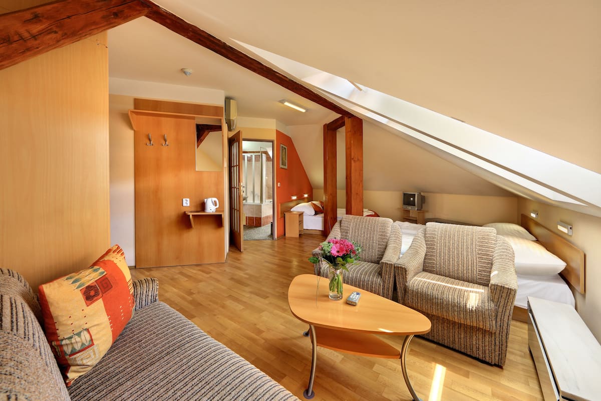 Um quarto acolhedor em estilo loft, com teto de madeira, um sofá, uma poltrona listrada e uma mesinha com um vaso de flores.