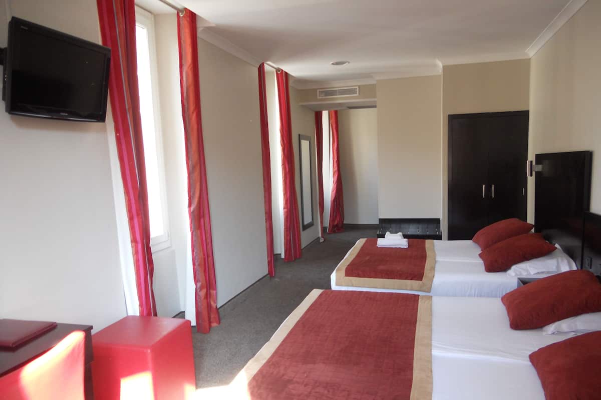 Quarto de hotel com duas camas, cortinas vermelhas, televisão e guarda-roupa.