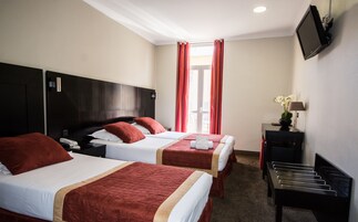 Quarto de hotel com duas camas, uma escrivaninha, televisão e janela com cortinas vermelhas.