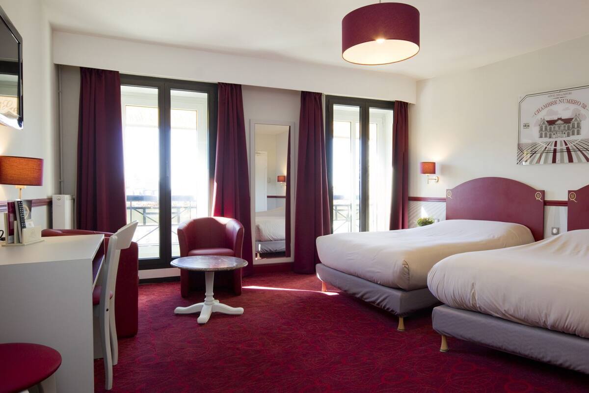 Quarto de hotel com duas camas, uma escrivaninha, uma cadeira, uma mesa e vista para a cidade.