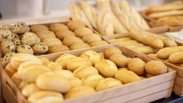 Diversos produtos de panificação em caixas de madeira, incluindo pão e doces.