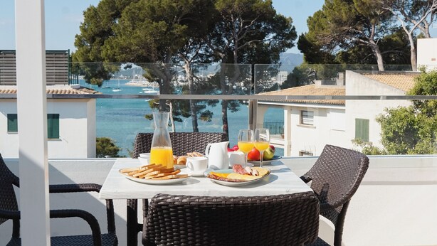 Varanda com mobiliário de vime, itens de café da manhã e vista para o mar e árvores.