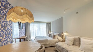 Quarto de hotel com uma mesa redonda, duas camas, um sofá, um candeeiro pendente e um espelho grande.
