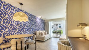 Uma sala de estar moderna com parede estampada, uma mesa de jantar redonda com cadeiras, um sofá e um abajur.