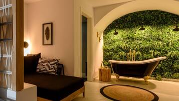 Quarto moderno com sofá preto, obra de arte com folha emoldurada, banheira antiga e parede verde com plantas.