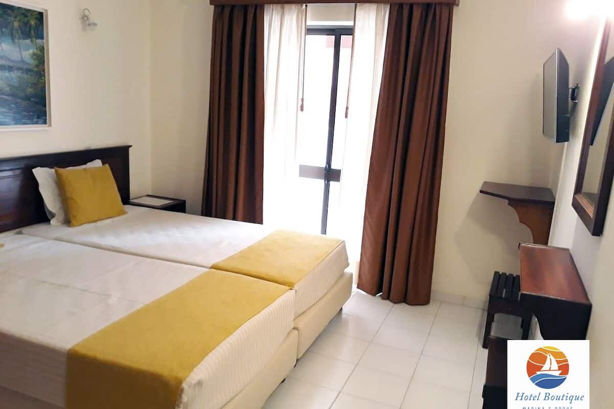 Quarto de hotel com uma cama grande, uma escrivaninha, uma cadeira, uma televisão e uma janela com cortinas.