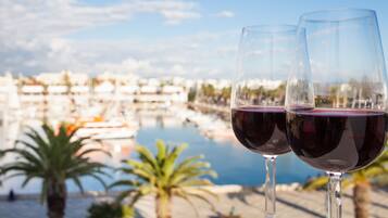 Duas taças de vinho tinto, com o cenário de uma marina com barcos e edifícios ao fundo.