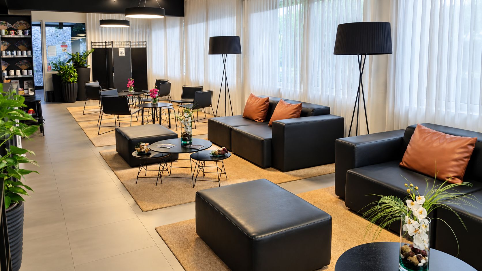 Um saguão de hotel moderno com sofás de couro, mesas redondas e luminárias de chão.