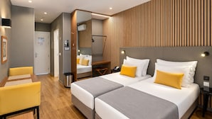Quarto de hotel com duas camas, cabeceira de madeira, uma escrivaninha pequena e uma cadeira.