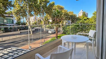 Uma varanda com mesa e cadeiras, com vista para uma rua com árvores e edifícios.