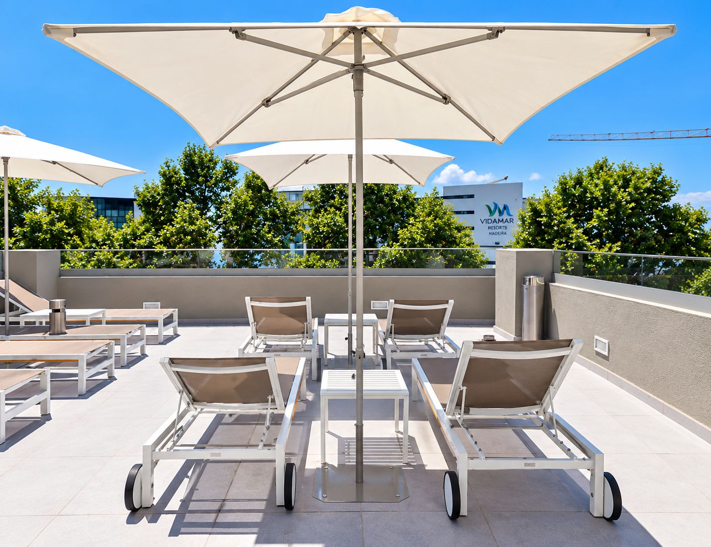 Terraço no telhado com espreguiçadeiras, mesas e guarda-sóis, com um aviso para Vidamar Resorts ao fundo.