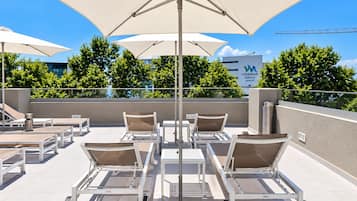 Terraço no telhado com espreguiçadeiras, mesas e guarda-sóis, com um aviso para Vidamar Resorts ao fundo.