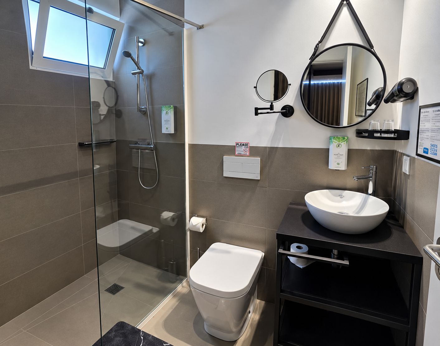 Casa de banho moderna com chuveiro envidraçado, sanita branca, lavatório com espelho em cima e um porta-toalhas.